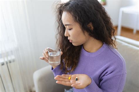 복통을 완화하기 위해 진통제를 복용하는 아시아 아픈 여자는 아침에 침대에 앉아 있습니다 고열로 침대에 누워있는 아픈 여자 감기