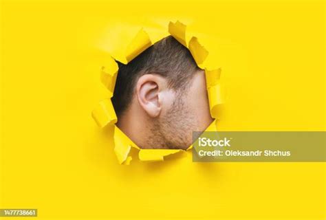 노란 종이의 찢어진 구멍을 통해 올바른 사람의 귀를 볼 수 있습니다 도청 간첩 가십 타블로이드 노란 언론의 개념 복사 공간이 있는 배경입니다 감각 지각에 대한 스톡 사진 및