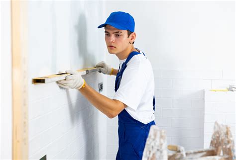 파란색 작업복의 남성 건축업자는 건물 수준을 사용하여 주어진 수직 벽과의 편차를 측정합니다 18 19세에 대한 스톡 사진 및 기타 이미지 Istock