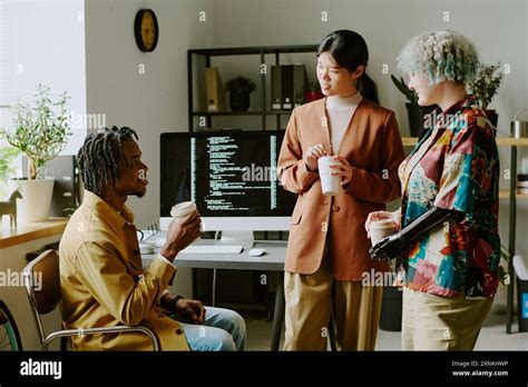 Group Of Three Diverse Gen Z Colleagues Wearing Stylish Outfits Chatting During Coffee Break In