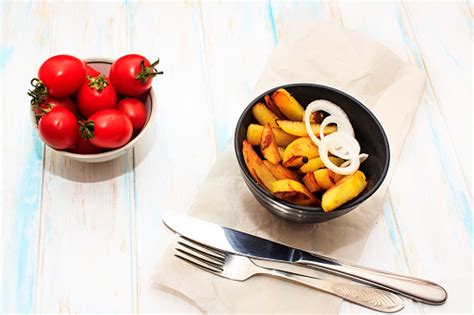 토마토와 양파를 사용한 집에서 만든 감자 요리 흰색 나무 배경에 향신료와 소금을 구운 감자 크 래 프 트 종이에 포크와 나이프 평면도 0명에 대한 스톡 사진 및 기타 이미지