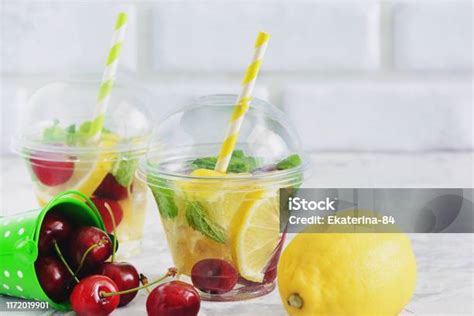 유기농 시트러스 베리 민트 잎을 곁들인 신선한 물 건강한 비건 음료 슬리밍 과 해독 개념 여름 레모네이드 클로즈업의 플라스틱 컵 테이블에 장식 양동이와 레몬에 잘 익은 체리