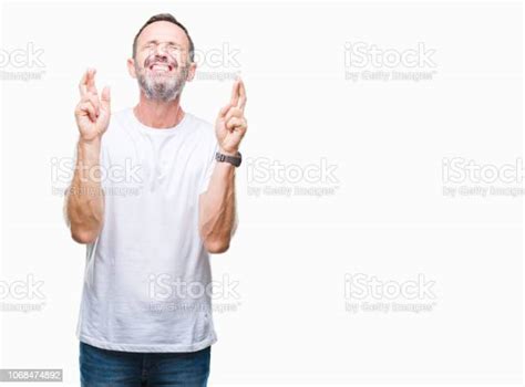 중 년 노인의 수석 사람 횡단 손가락 희망 및 눈을 감고 미소 격리 된 배경 위에 흰색 T셔츠를 입고 행운과 미신의 개념입니다