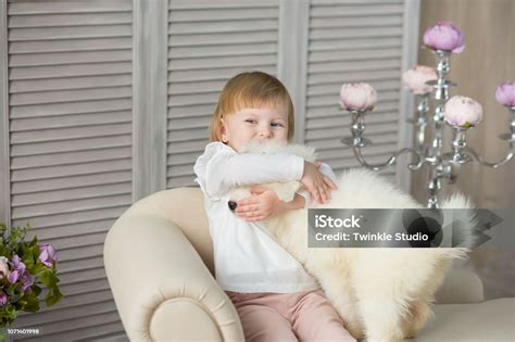 금발 아가씨의 허스키 강아지와 함께 재생 합니다 금발 머리 귀여운 드레스를 입고 로얄 복고풍 안락의 자 소파 소파에 앉아있는 동안 새 미 하얀 강아지와 함께 스튜디오