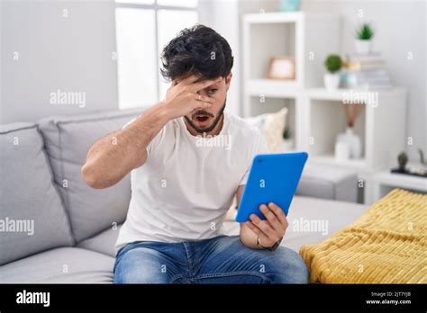 Hispanic Man With Beard Using Touchpad Sitting On The Sofa Peeking In