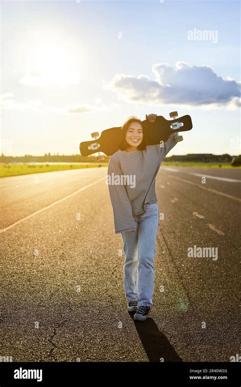Young Asian Woman Standing With Longboard On Sunny Road Skating In