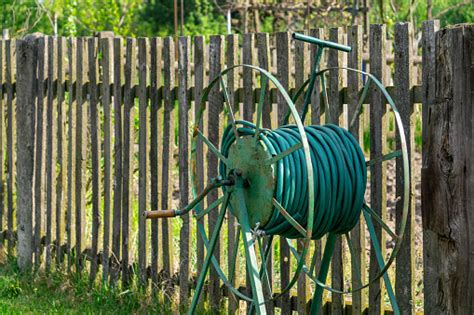 오래된 복고풍 스타일은 정원의 잔디밭에 세워진 나무 울타리를 배경으로 정원 호스와 함께 서 있습니다 여름과 봄의 건조한 날에 채소밭에 물을 줍니다 0명에 대한 스톡 사진 및