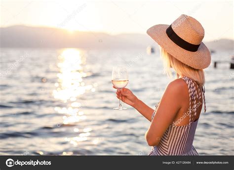 Woman Holds Wineglass At Background Of Sunset Sea Or Ocean Blond Girl