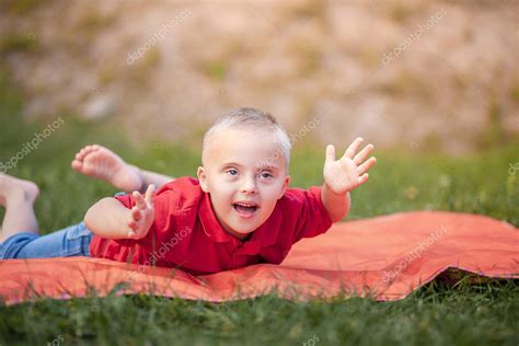 Un Niño Con Síndrome De Down Yace En El Parque Sobre Una Alfombra
