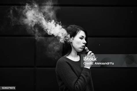 Vape 십대 겨울에 거리에서 현대 갈색 배경 맞은 편에 전자 담배를 흡연 빨간 스웨터에 젊은 예쁜 흰색 백인 소녀 나쁜 습관 연기 물리적 구조에 대한 스톡 사진 및 기타