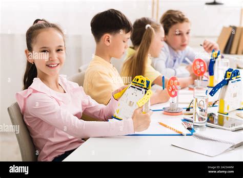 Stem Education Happy Girl Creating Robot At Classroom Smiling To Camera With Classmates On