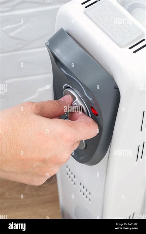 Woman Hand Turning The Thermostat Knob Of A Home Electric Oil Heater White Oil Filled Radiator