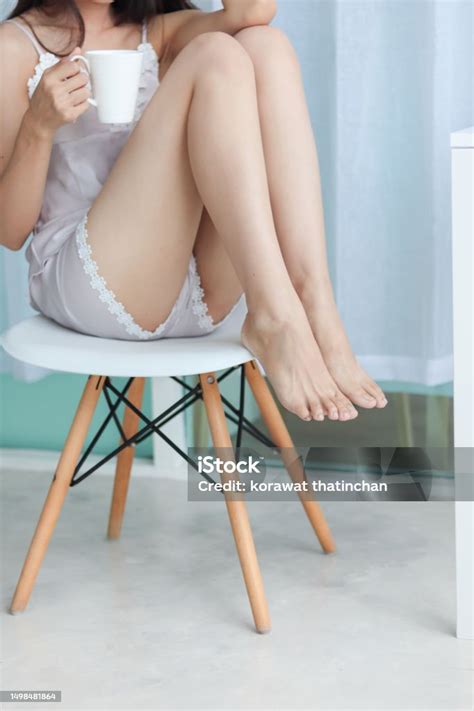 잠옷을 입은 젊은 여성은 아침에 커피 한 잔과 함께 창가 의자에 앉아 커피를 마시고 아침에 아름다운 풍경을 감상한다 몸을