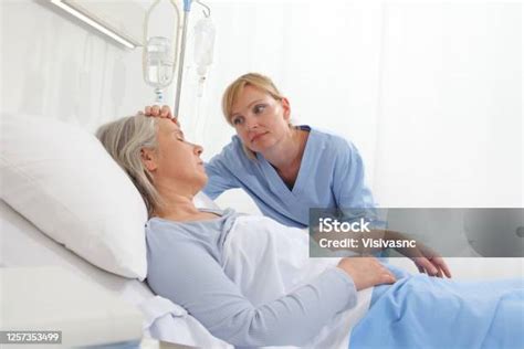 간호사는 병원 방 침대에 누워 있는 안락한 노인 여성을 데리고 그녀를 쓰다듬고 물방울 바늘이 있는 팔을 잡고 외로움과 노령질병의