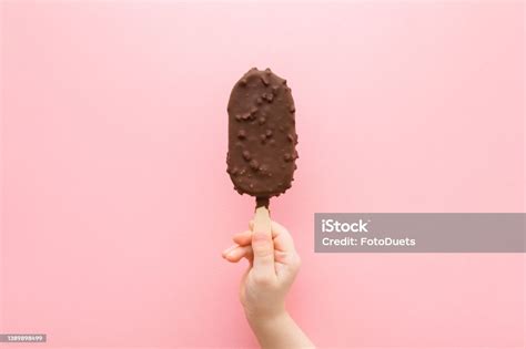 아기 소녀는 밝은 분홍색 테이블 배경에 견과류와 초콜릿 유약으로 아이스크림을 들고 있습니다 파스텔 색상 근접 촬영 아이들은