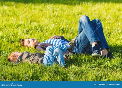 Cheerful Two Brothers Lie On The Grass In The Park And Play In Funny