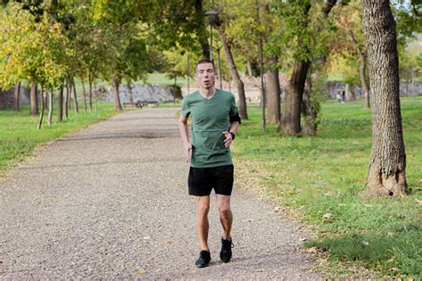 정신 건강 및 자기 관리 활동의 일환으로 공공 공원에서 야외에서 부드러운 일상 운동을하는 행복한 운동 중반 성인 남성 그는 운동복과 스마트 워치를 착용하고 조깅을하고