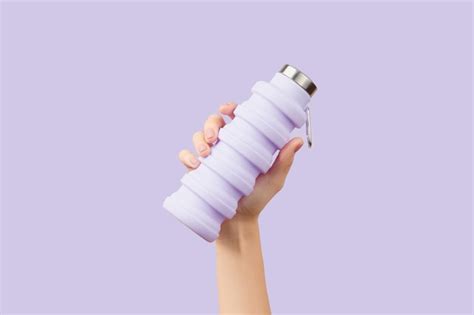 Premium Photo Womans Hand Holding Collapsible Reusable Lilac Water Bottle On Purple Background