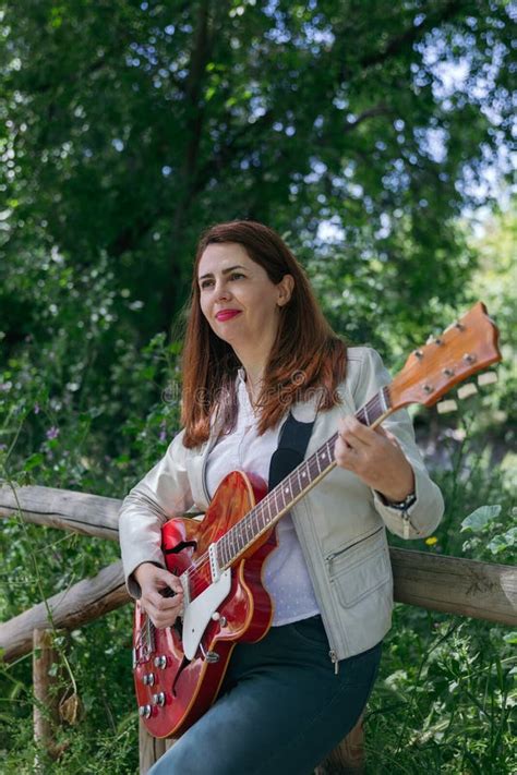 Mature Woman Playing Her Red Acoustic Guitar In An Outdoor Park