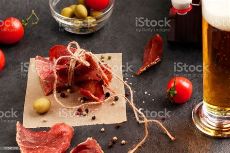 맥주 에 대한 천연 간식 매운 육포 조각은 어두운 배경에 양피지 종이에 꼬기와 묶여 조미료와 거친 소금 붉은 체리 토마토 올리브