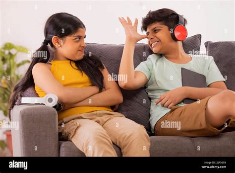 Young Brother Teasing His Sister While Sitting On Sofa With Digital