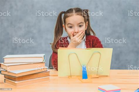 회색 배경에 어린 소녀 여학생입니다 이 기간 동안 그녀는 책을 읽는 동안 그녀의 숙제를 수행한다 흰색 셔츠와 빨간 재킷을 입고