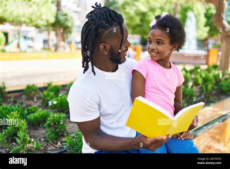 Father And Daughter Reading Book Sitting Together On Bench At Park