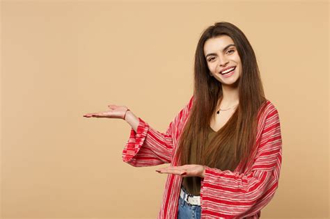 캐주얼에서 쾌활 한 젊은 여자의 초상화 카메라를 찾고 스튜디오에서 파스텔 베이 지 배경에 고립 된 손을 옆으로 가리키는 사람들은