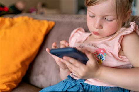 전화를 사용하는 아이 금발 머리를 가진 소녀는 집에서 스마트 폰으로 재생됩니다 손에 아이와 스마트 폰 디지털 태블릿을 가진