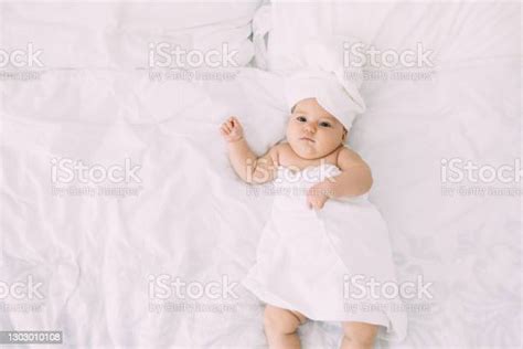 6 개월 된 소녀는 그녀의 머리와 몸에 수건을 가진 침대에 누워있다 위생 및 유아 관리 개념 가정의 방에 대한 스톡 사진 및
