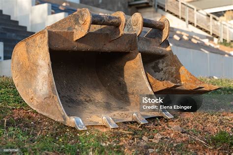 주택 건설 현장의 바닥에 있는 녹슨 굴착기 부착물 미니 굴삭기 및 지형 작업은 신선한 붉은 토양과 계단식 콘크리트 구조물로 진행 중입니다 건설 기계류에 대한 스톡 사진 및