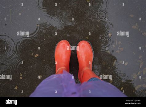 Woman Wearing Red Rubber Boots Standing In Rippled Puddle Top View