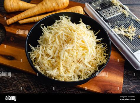 Bowl Of Shredded Parsnips On A Wood Cutting Board Whole And Shredded