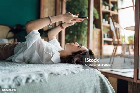 침대에 누워있는 동안 스마트 폰으로 온라인으로 쇼핑하는 편안한 젊은 아시아 여성 청소년 문화 일상 생활의 기술 인터넷 데이트에