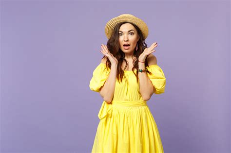 노란색 드레스에 충격 젊은 여자 여름 모자 입을 열어 스튜디오에서 파스텔 바이올렛 벽 배경에 고립 된 손을 확산 사람들은