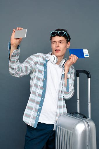 회색 벽 관광 개념에 고립 된 남자는 여권과 티켓을 들고 수하물을 들고 서있는 전화로 장난스럽게 카메라에 장난을 치는 셀카를