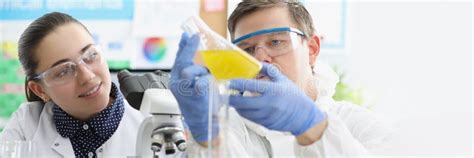 Laboratory Workers Man And Woman Examine Yellow Liquid In Flask Stock