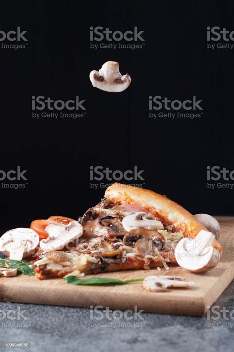 햄 토마토 치즈 양파 허브가 있는 커팅 우드 보드에 수제 이탈리아 피자에 떨어지는 버섯 조각이 어두운 돌 슬레이트 테이블에 놓여