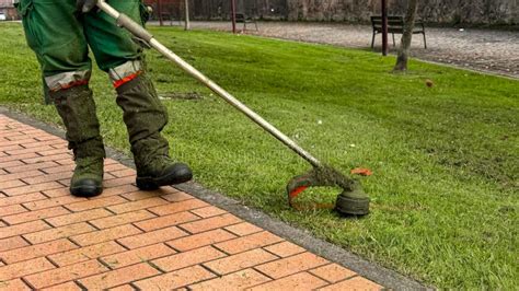 Worker Trimming Grass With String Trimmer On Pathway At Park Stock