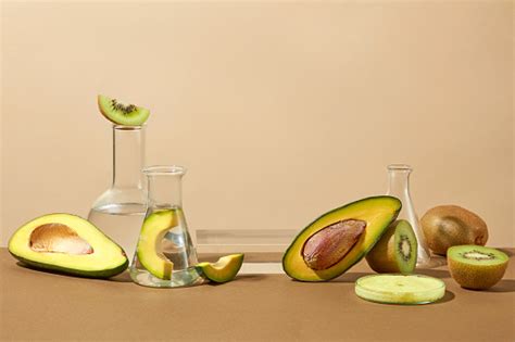 밝은 갈색 배경에 투명한 액체가 있는 여러 개의 신선한 키위 아보카도 및 실험실 기구가 포함된 갈색 조리대가 있는 갈색 톤 사진