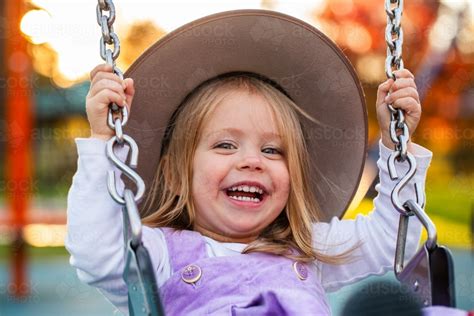 Image Of Happy Little Australian Girl Laughing As She Swings On Swing