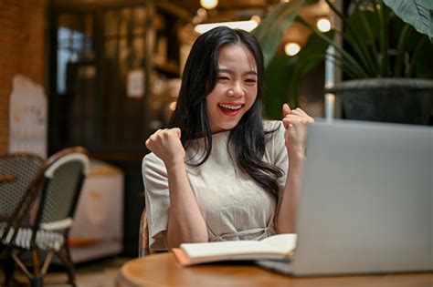 쾌활한 아시아 여성이 노트북 화면을 보며 자신의 성공을 기뻐하고 축하하고 있다 좋은 소식에 대한 스톡 사진 및 기타 이미지