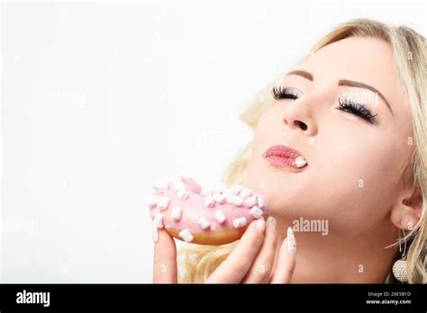 Blonde Woman Enjoys A Pink Frosted Donut With Marshmallows Indulging