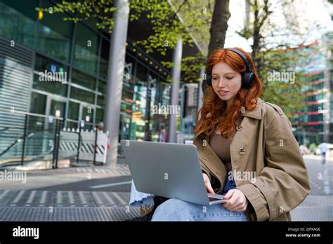 Teen Redhead Hipster Girl Wearing Headphones Using Laptop On City Urban