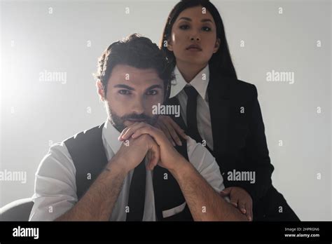 Stylish Interracial Couple In Formal Wear Looking At Camera On Grey