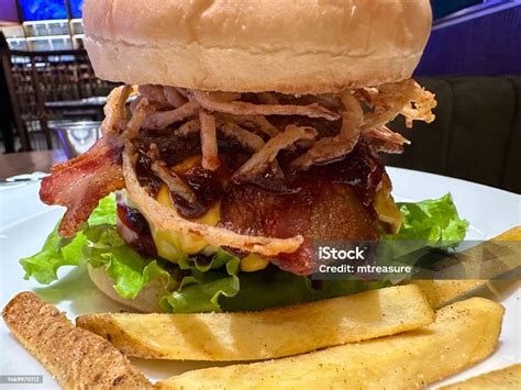 감자 튀김 칩 씨없는 버거 롤빵 베이컨 녹은 치즈 토마토 양상추 및 양파의 일부와 함께 제공되는 미식가 패스트 푸드 테이크 아웃 더블 치즈 버거의 클로즈업 이미지 전경에