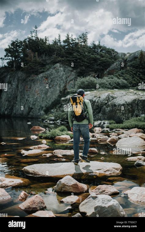 Rear View Of Hiker With Backpack Walking On Rocks Over Stream Stock