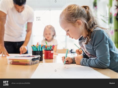 Girl Using Felt Tip Pen In Drawing Class With Classmate And Teacher In Background Stock Photo