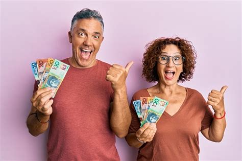 아름다운 중년 부부는 오픈 입으로 행복 미소 측면에 엄지 손가락을 가리키는 호주 달러를 들고 손에 대한 스톡 사진 및 기타