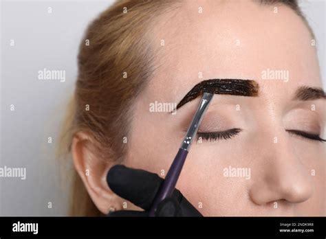 Beautician Applying Tint During Eyebrows Correction Procedure On Light Grey Background Closeup